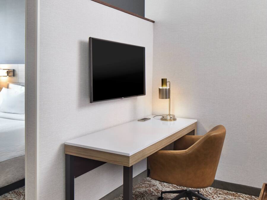 Quarto de hotel com cama, escrivaninha, cadeira, televisão e abajur.