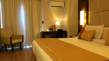 Quarto de hotel com cama, escrivaninha, cadeira e ar condicionado.