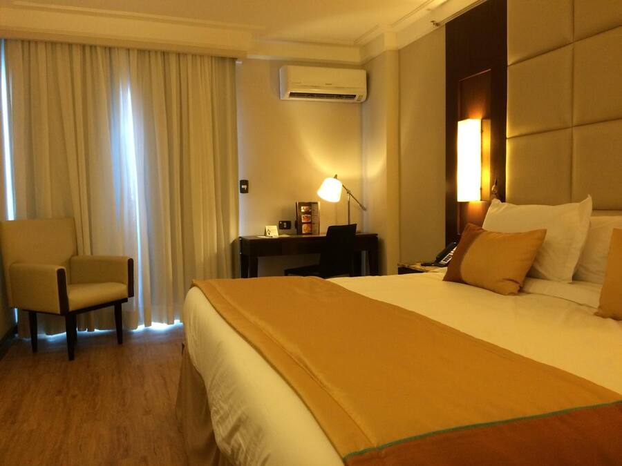 Quarto de hotel com cama, escrivaninha, cadeira e ar condicionado.