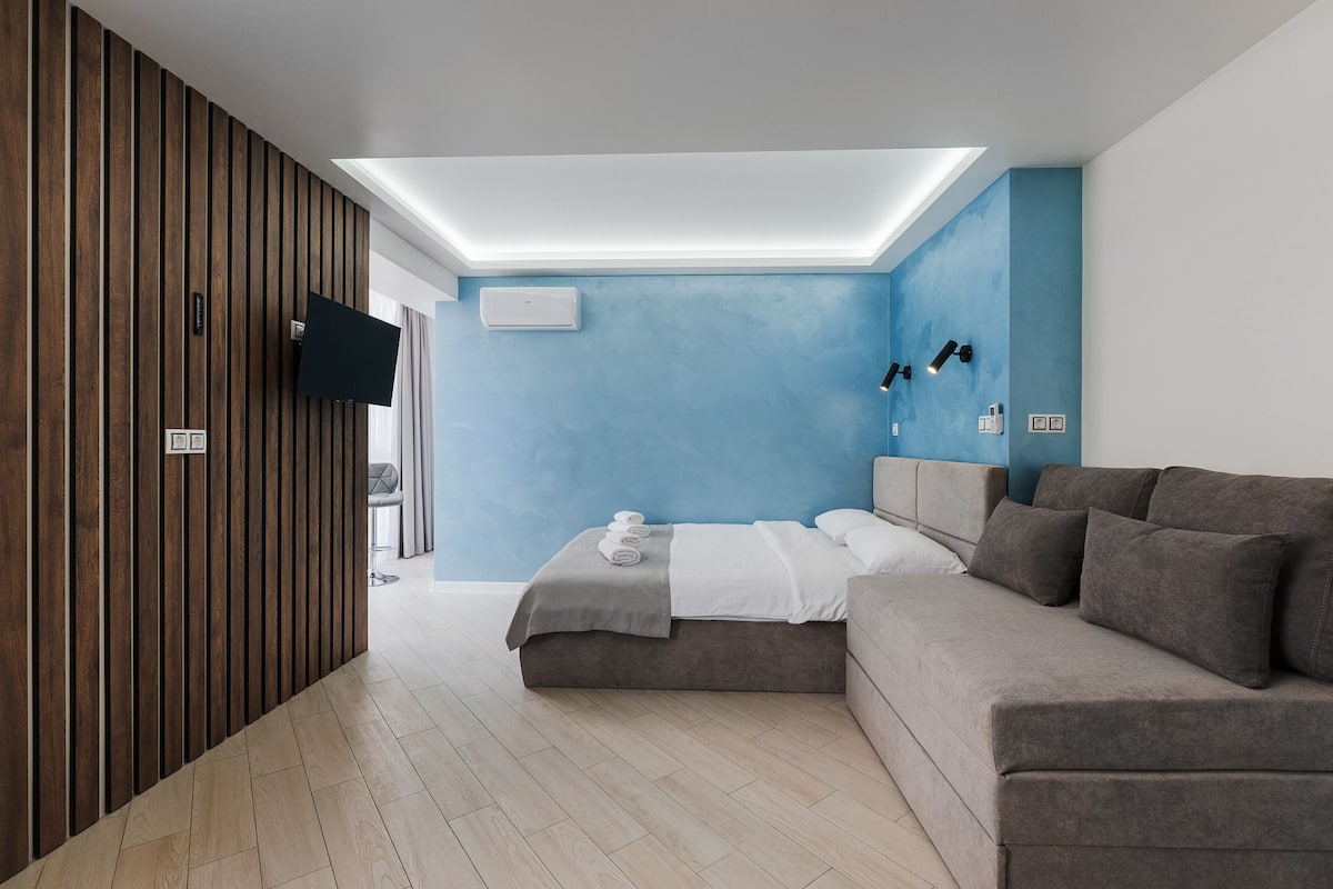 Quarto moderno com cama, sofá, televisão e claraboia.