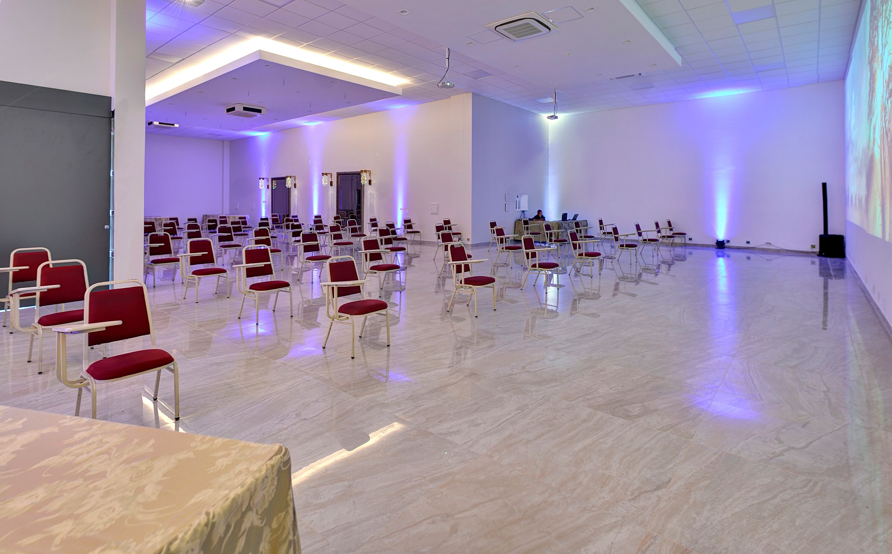Uma sala de conferências ampla, com fileiras de cadeiras vermelhas e um amplo telão.
