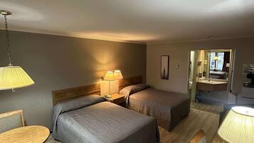 Quarto de hotel com duas camas, uma escrivaninha de madeira, uma cadeira e um abajur.
