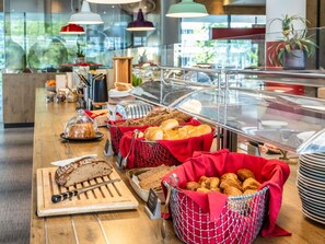 Uma área de buffet com diversos pães e doces dispostos em cestas e numa tábua de corte.