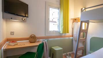 Quarto de hotel com uma cama, escrivaninha com cadeira, televisão na parede, janela com cortinas e uma cama beliche.