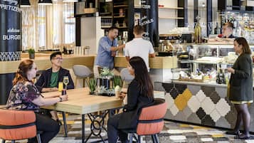 Um café moderno com mesas, cadeiras, um balcão de bar e um balcão de atendimento.