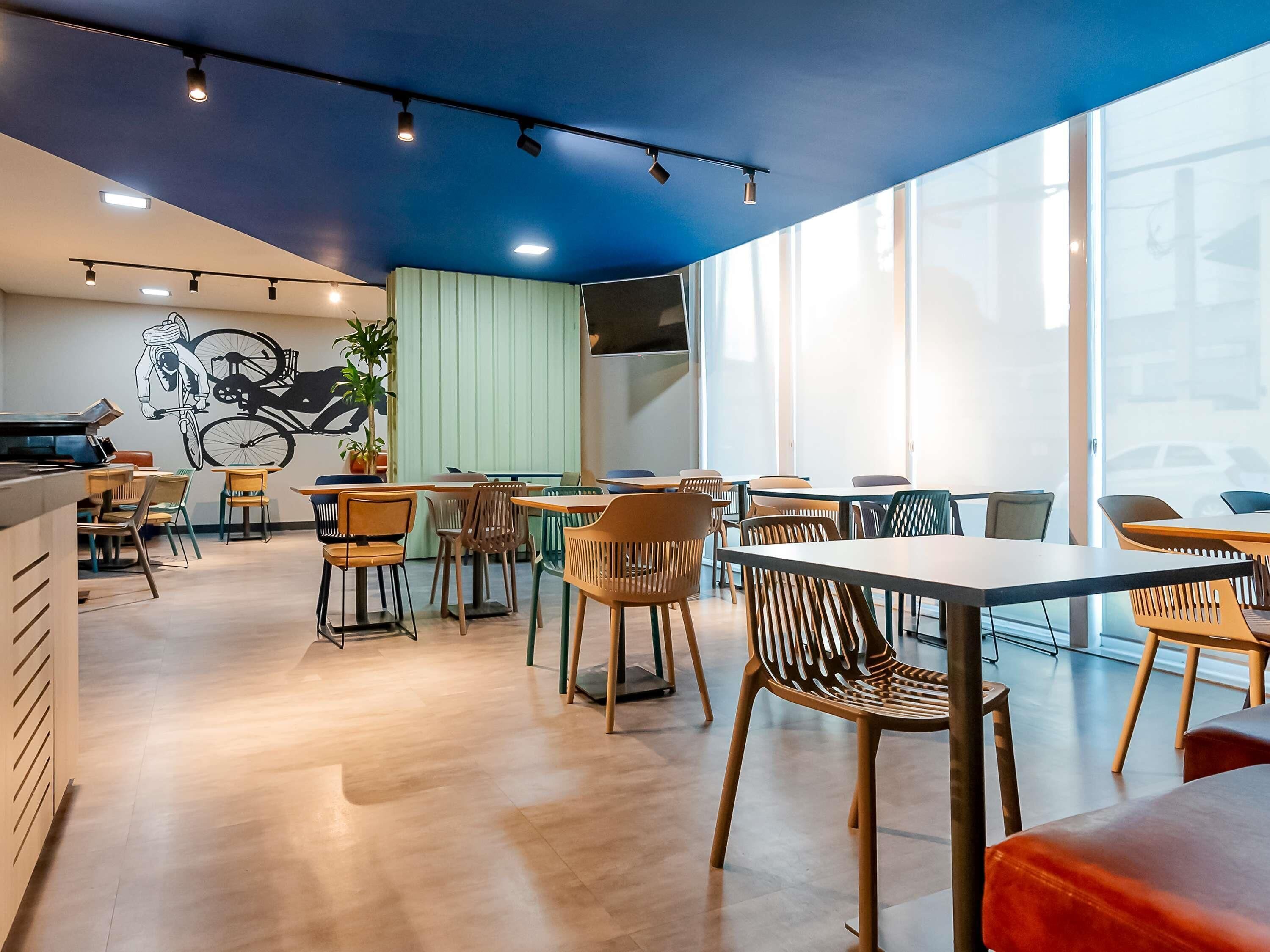 Um interior moderno com mesas e cadeiras de madeira, uma janela grande e um mural na parede.