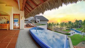 Um resort com uma grande piscina infinita, uma construção com telhado de palha e vista para o pôr do sol entre palmeiras.