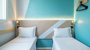 Quarto de hotel com duas camas, cabeceira de madeira, parede em tom de verde-água e um cabide preto na parede.