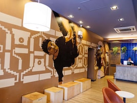 Um hall de hotel moderno com um mural geométrico na parede, assentos de madeira e um balcão de recepção.