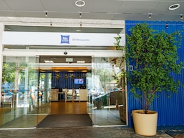 Entrada moderna de hotel com portas de vidro, balcão de recepção e planta em vaso.
