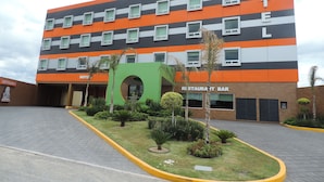 Hotel com design moderno, destacando uma entrada verde, um bar-restaurante e diversos quartos.