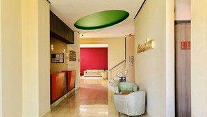 Um saguão de hotel com balcão de recepção, parede vermelha, escadaria e área de estar.