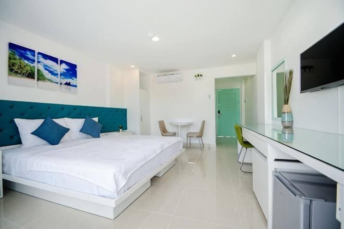 Quarto de hotel com uma cama, uma escrivaninha, uma cadeira, uma televisão e uma porta.