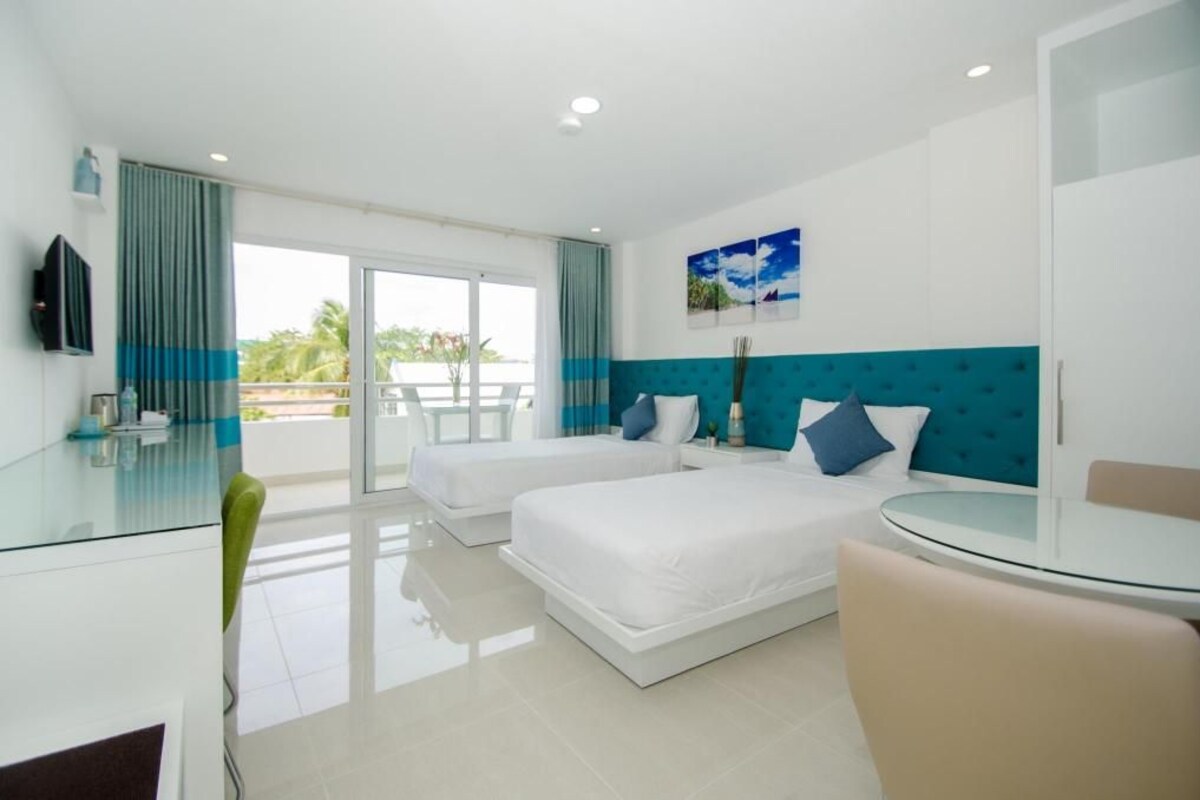 Quarto de hotel com duas camas, uma mesa de vidro, uma cadeira e varanda com vista.