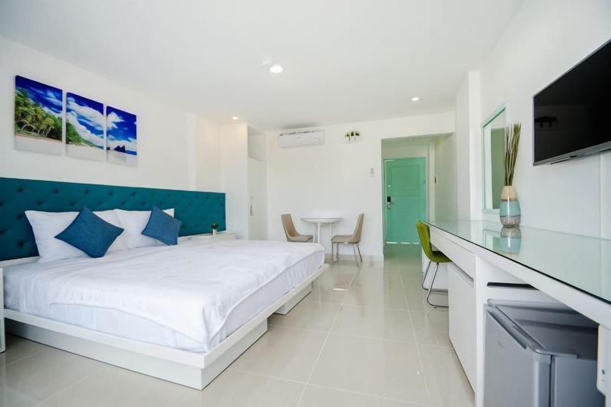 Quarto de hotel com uma cama, uma escrivaninha, uma cadeira, uma televisão e uma porta.