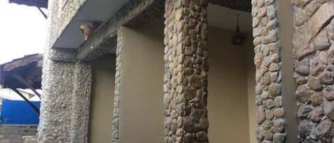 Fachada de pedra com colunas, telhado plano e uma pequena varanda.