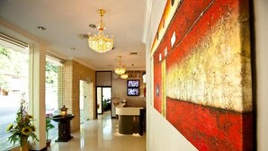 Um saguão de hotel com uma mesa de recepção, um candelabro e uma grande pintura abstrata na parede.