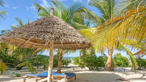 Uma praia com um guarda-sol de palha e duas cadeiras de praia azuis.