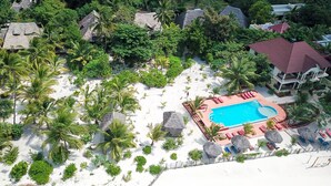 Vista aérea de um resort com piscina, cercado por palmeiras e edifícios com telhados de palha.