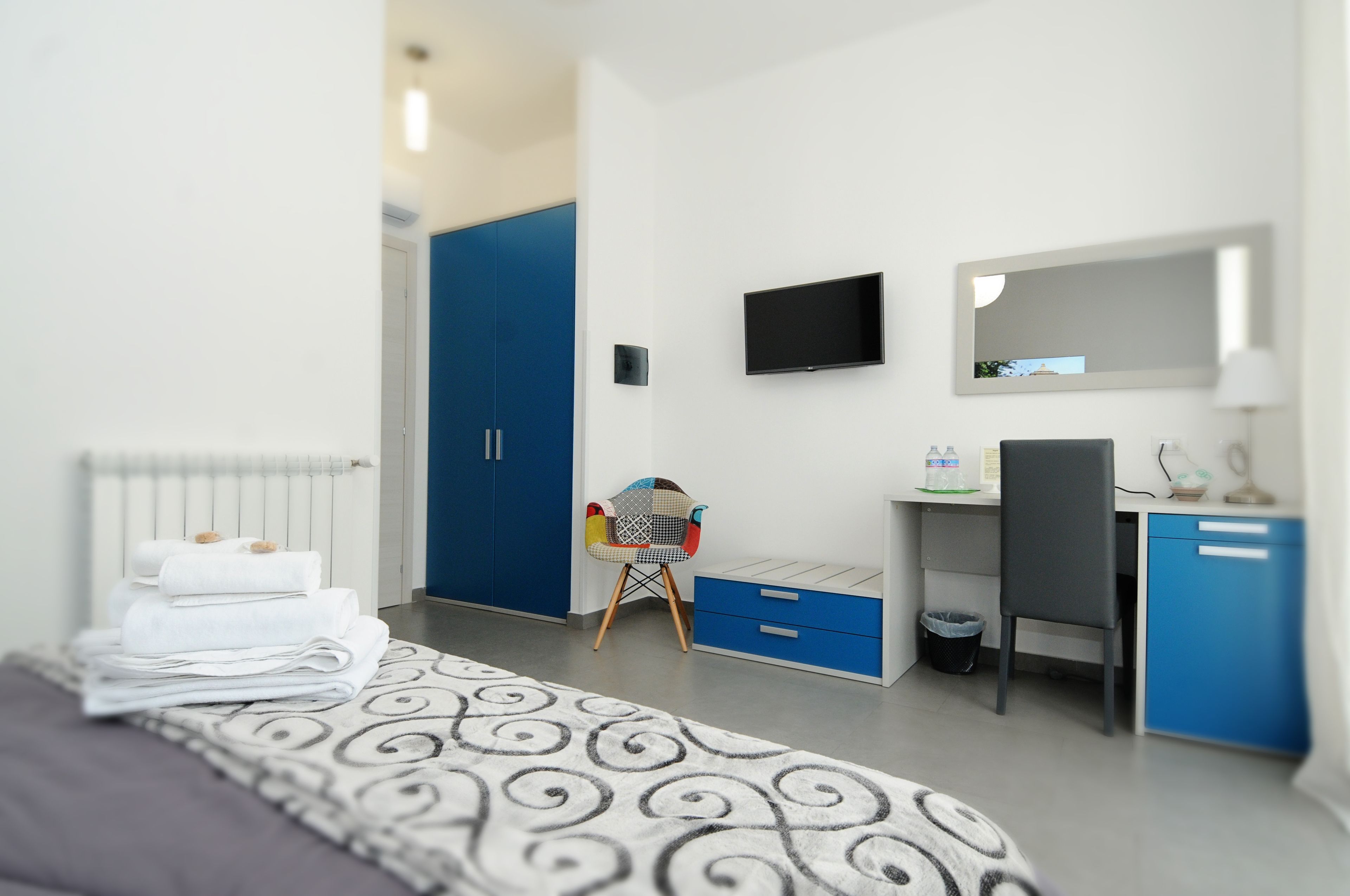 Quarto moderno com cama, escrivaninha, cadeira, televisão e guarda-roupa.