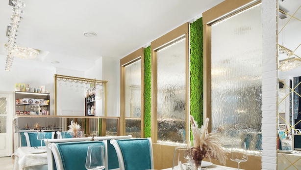 Restaurante com cadeiras azul-esverdeadas, mesas brancas e um jardim vertical verde.
