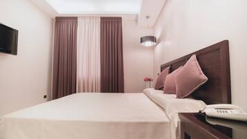 Quarto de hotel com cama, mesa de cabeceira com telefone, luminária e televisão na parede.