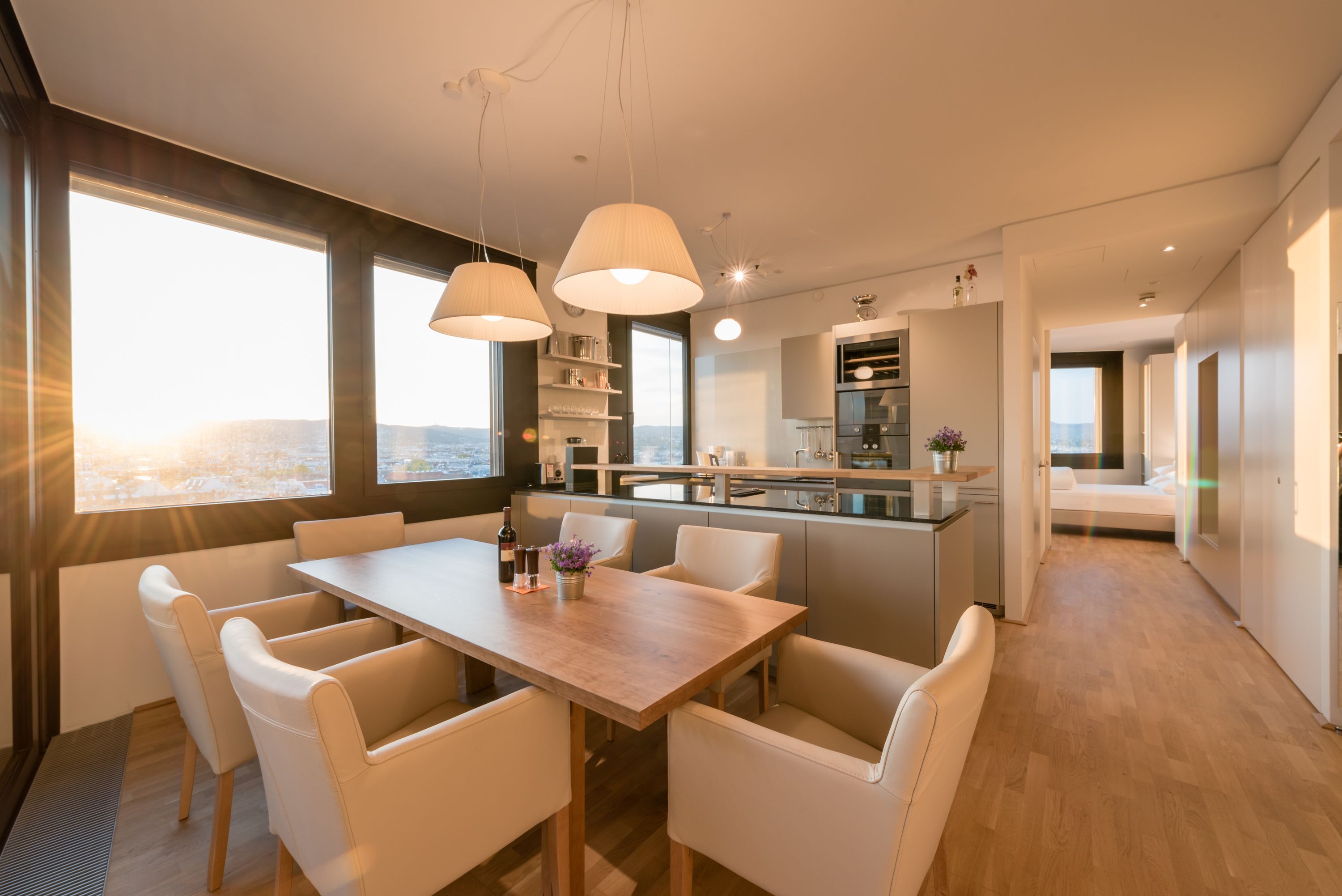 Cozinha moderna com área de jantar, grandes janelas e vista para a cidade.
