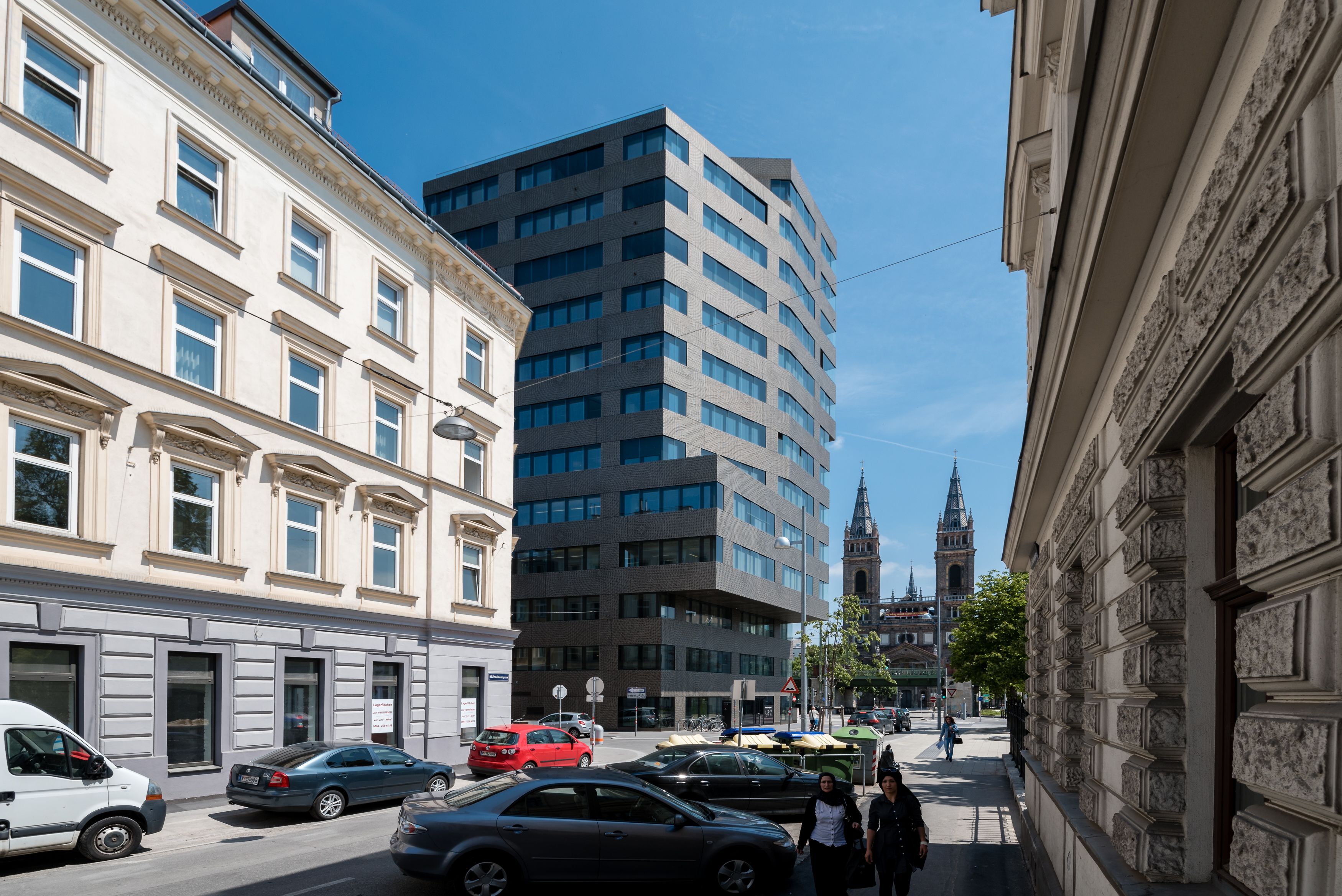Vista da rua com mistura de edifícios modernos e históricos, incluindo uma torre do relógio imponente.