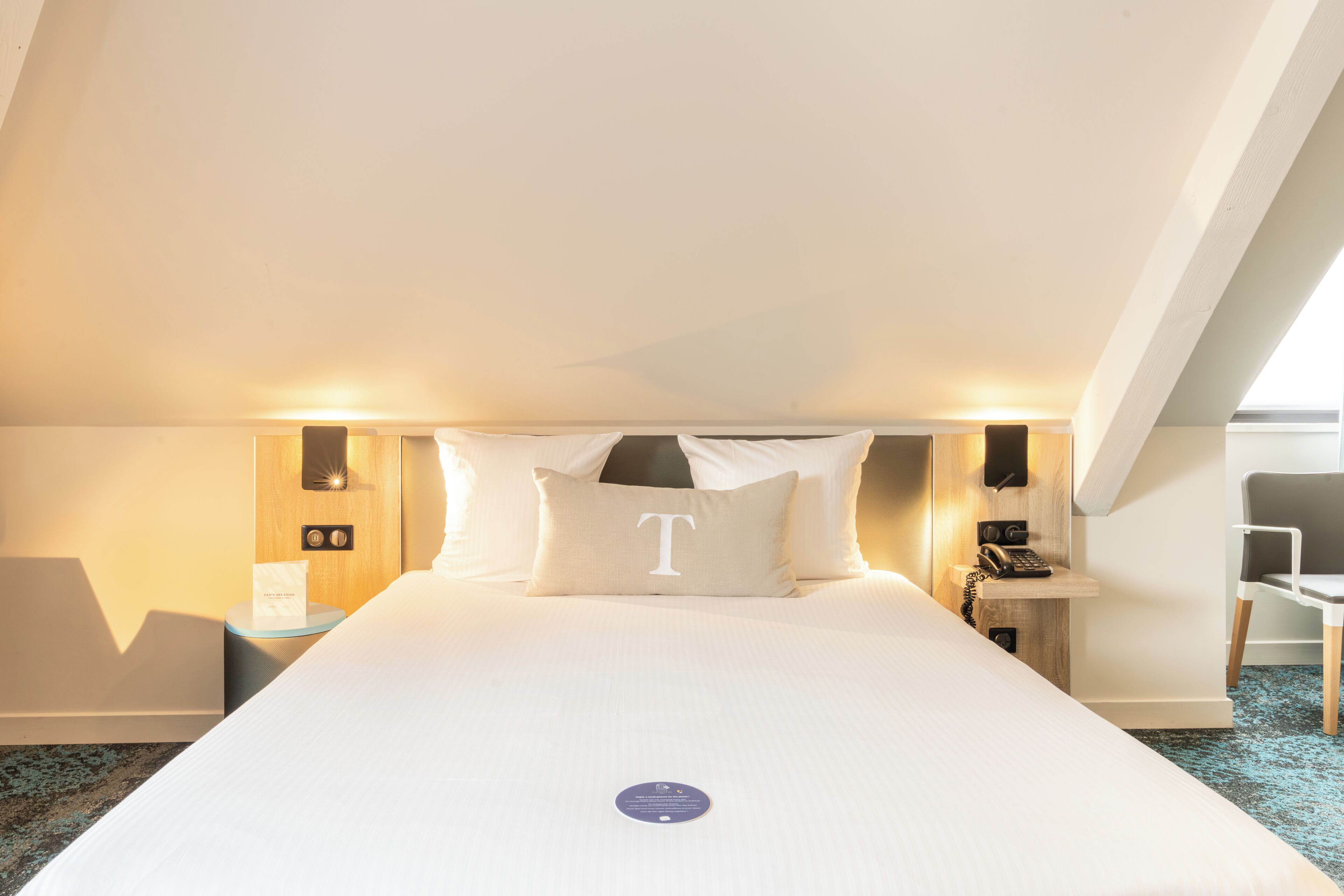 Quarto de hotel com uma cama grande, uma mesa com telefone e uma cadeira.