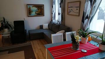 Uma sala de estar com sofá, uma mesa de jantar com cadeiras, um candelabro e duas pinturas na parede.