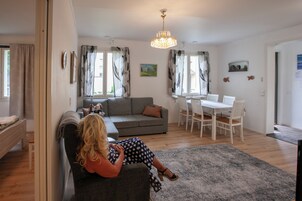 Uma sala de estar com sofá, mesa de jantar com cadeiras, lustre e um quadro na parede.
