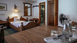 Uma cama de madeira com uma mesa de cabeceira, uma mesa de madeira com uma bandeja de garrafas de água, um ventilador e um espelho na parede.