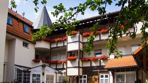 Um hotel europeu tradicional com telhado em duas águas, várias varandas com flores vermelhas e uma torre imponente.