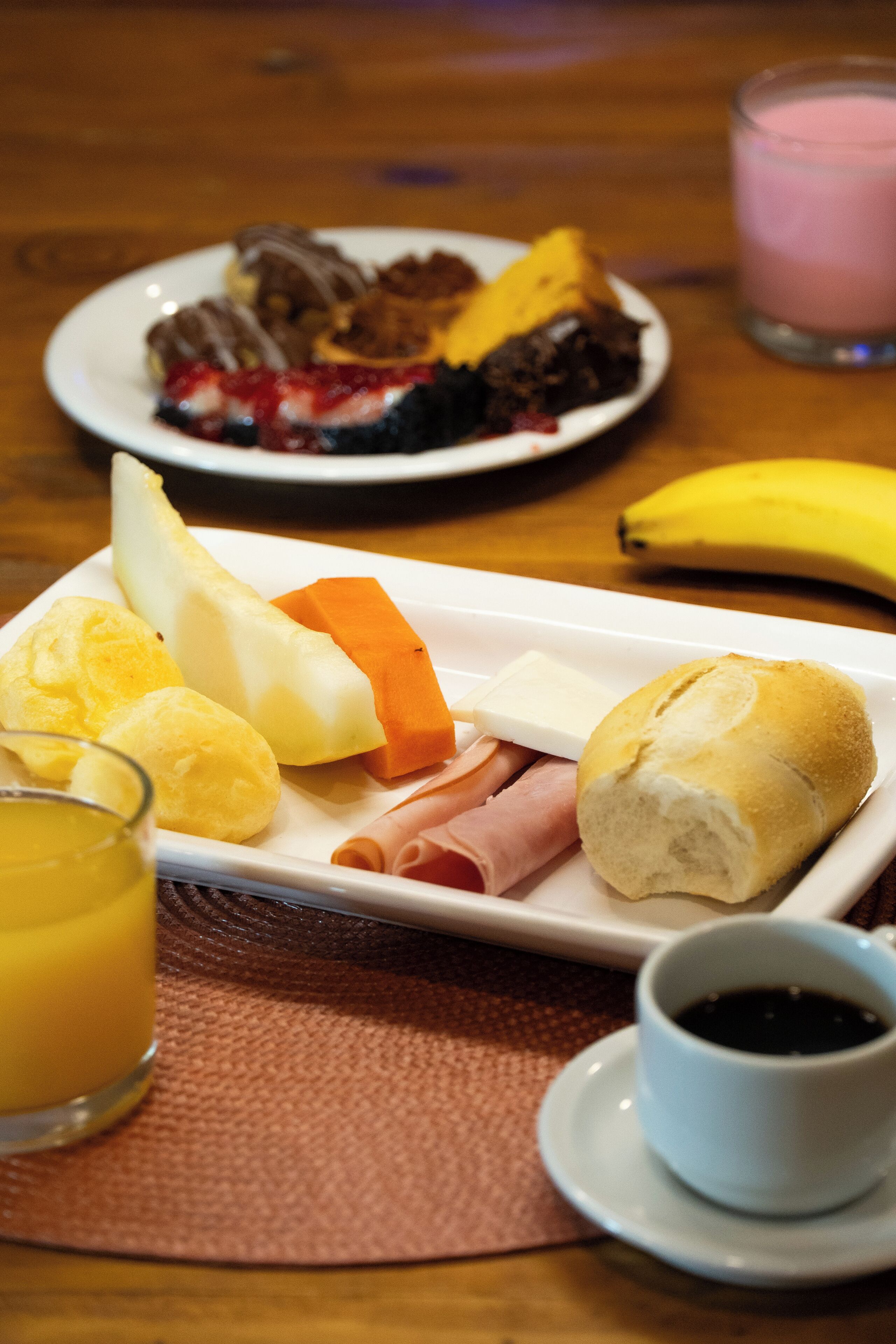 Bandeja de café da manhã com ovos, queijo, presunto, pão e uma banana sobre uma mesa de madeira.