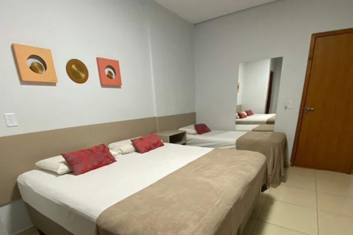 Quarto de hotel com três camas, uma porta de madeira e um espelho na parede.