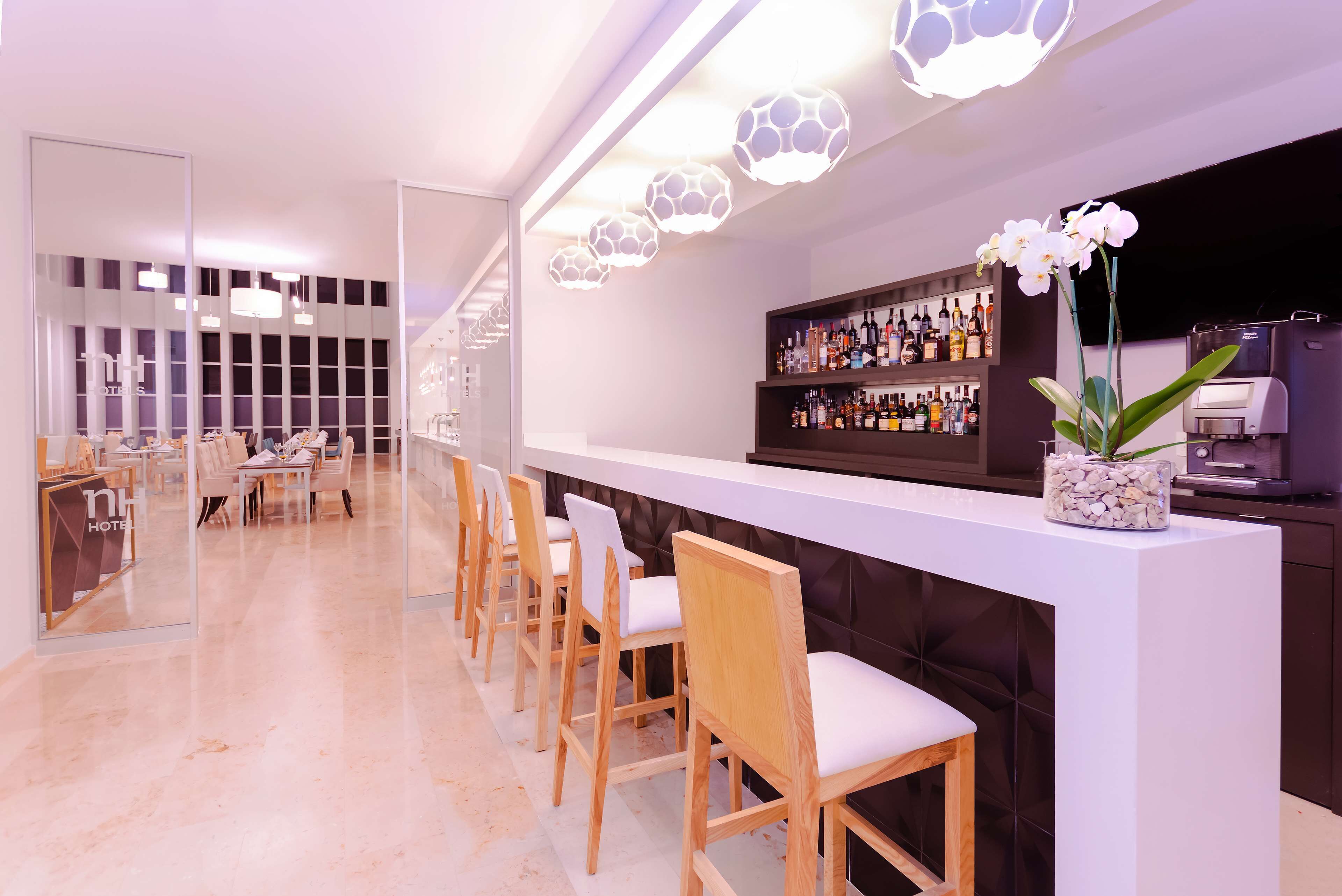 Uma área de bar moderna com balcão branco, cadeiras de madeira e diversos frascos.