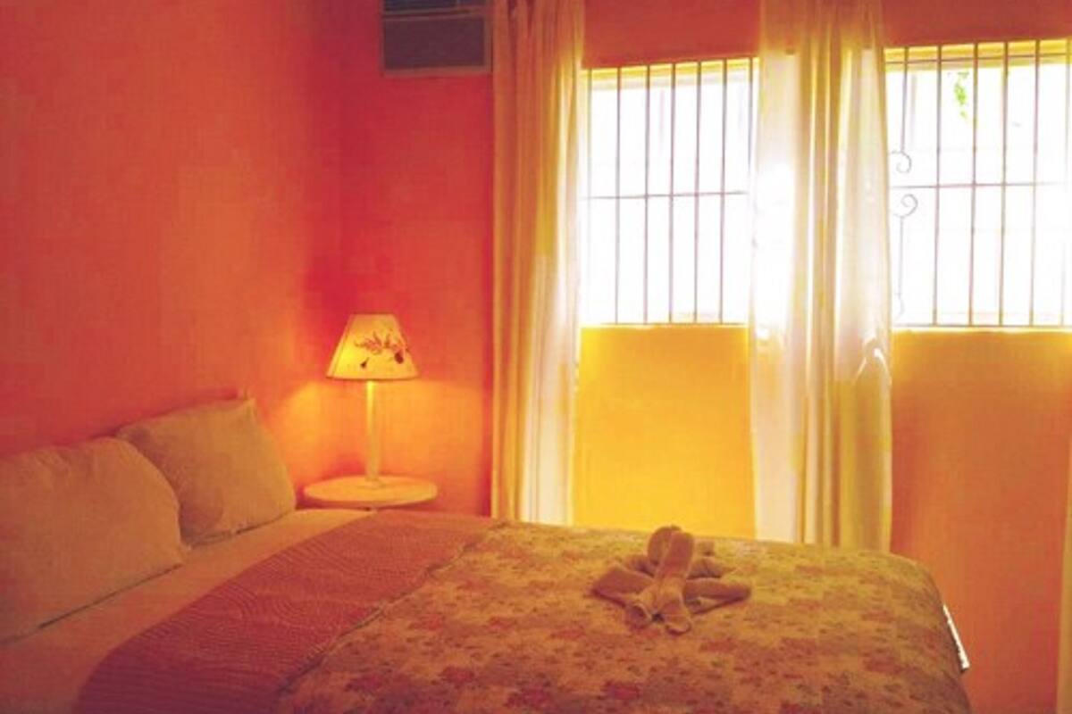 Quarto com cama, luminária e janela com cortinas.