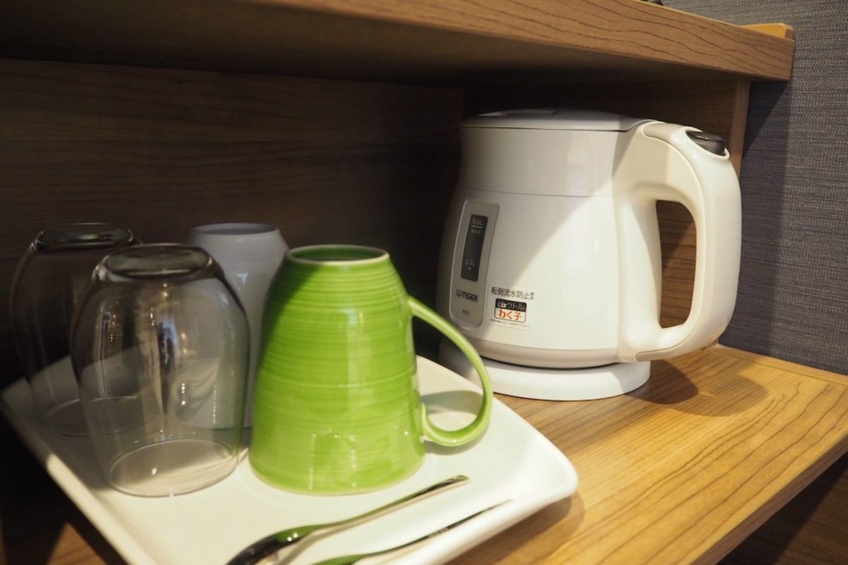 Uma prateleira com uma caneca branca, uma caneca verde e um prato com uma colher.