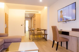 Uma sala de estar moderna com sofá, mesa de centro, TV fixada na parede e área de jantar com mesa e cadeiras.