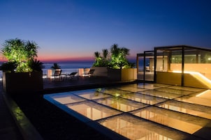Terraço no telhado com piso de vidro, área de estar e estrutura envidraçada.