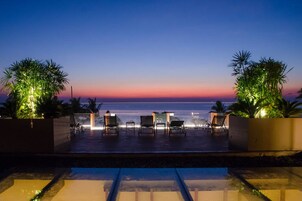 Área da piscina com espreguiçadeiras e vista para o oceano ao entardecer.