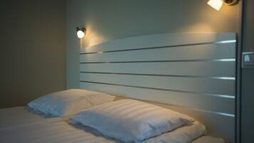 Quarto com cama, duas almofadas e luminária na parede.