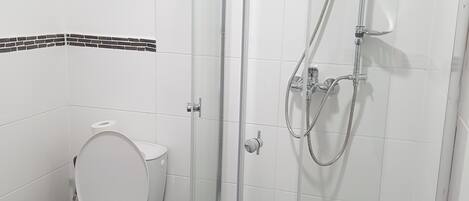 Casa de banho moderna com sanita, cabine de chuveiro com parede de vidro e parede revestida a mosaico branco.