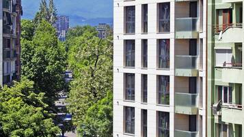 Edifício residencial com vários andares, varandas, área de estacionamento e árvores ao primeiro plano.