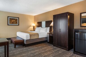 Quarto de hotel com cama, mesas de cabeceira, escrivaninha, guarda-roupa e televisão na parede.