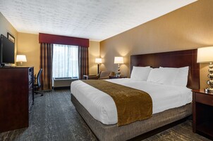 Quarto de hotel com uma cama grande, duas luminárias de cabeceira, uma escrivaninha com televisão e uma cadeira.