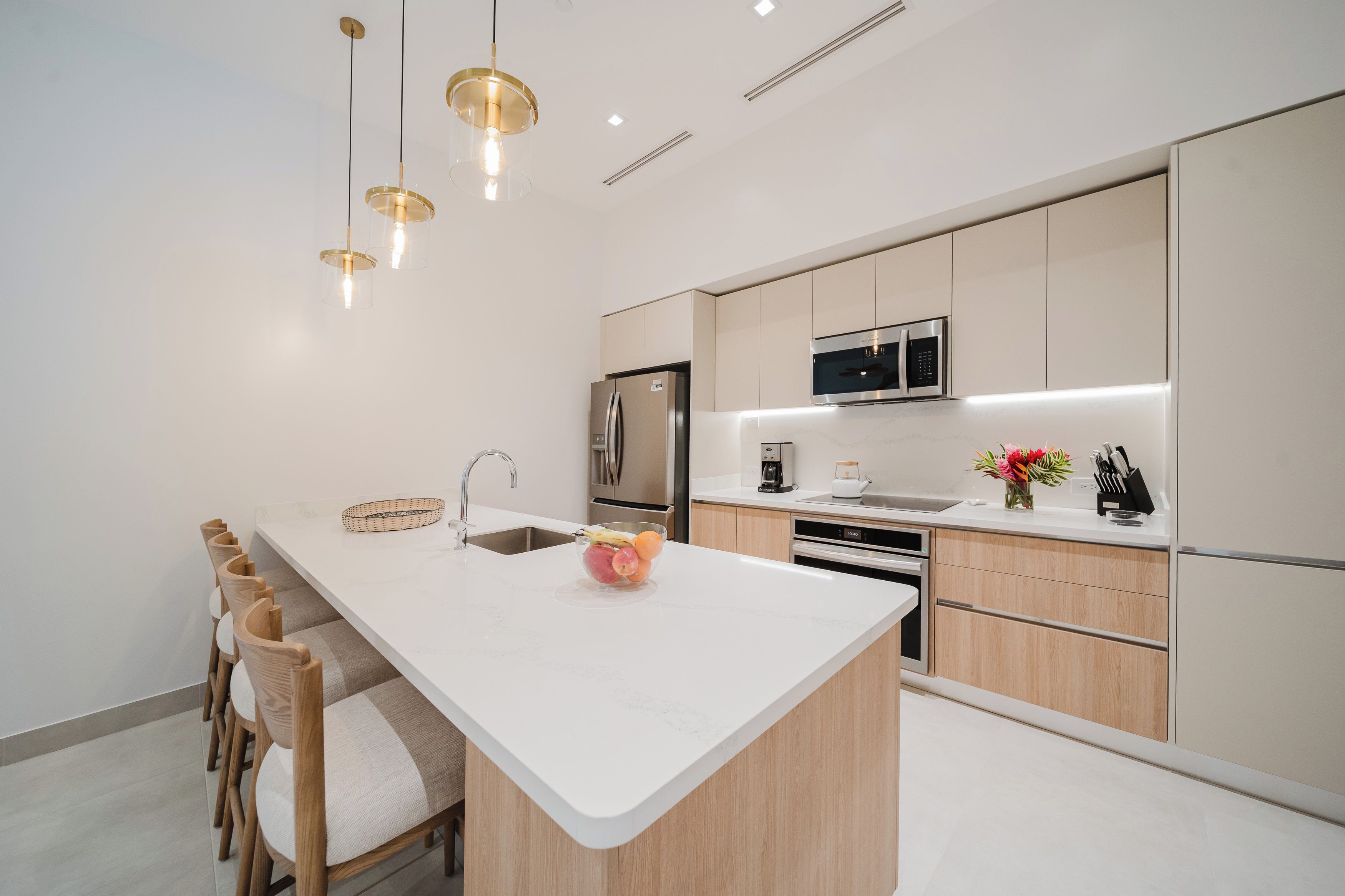 Cozinha moderna com ilha central, eletrodomésticos de aço inoxidável e iluminação pendente.