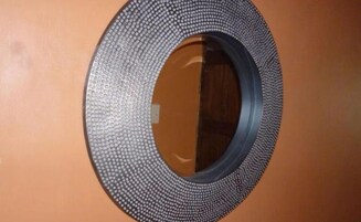 Um objeto circular com superfície texturizada e um orifício central, fixado numa parede lisa.