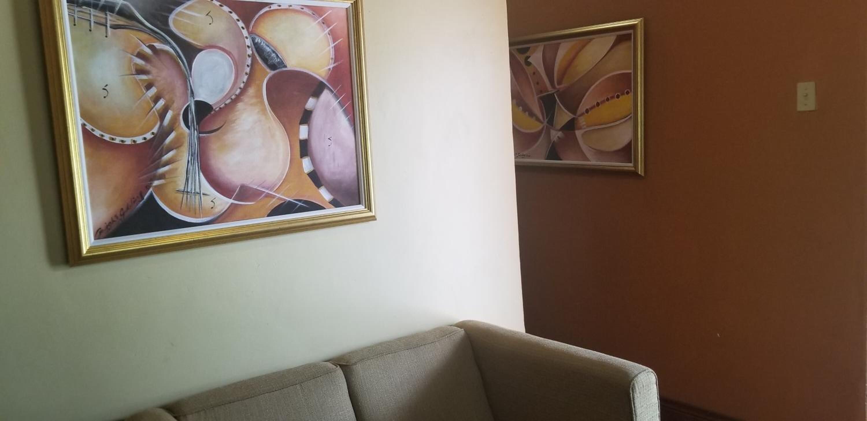 Um quarto com um sofá bege e duas pinturas abstratas na parede.
