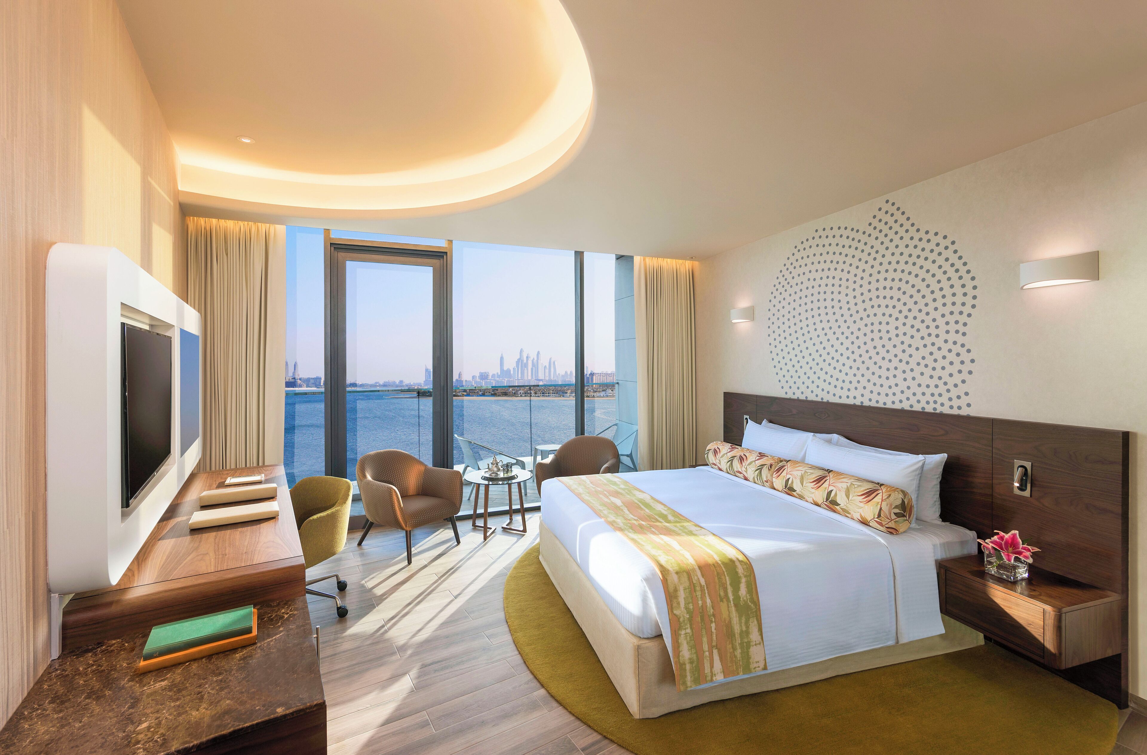 Quarto de hotel com uma cama grande, uma escrivaninha, uma televisão e vista para a cidade, com paisagem urbana pela janela.